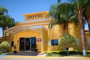 Um hotel com fachada amarela, um letreiro 'HOTEL' acima da entrada e uma placa 'Zar Hoteles'.