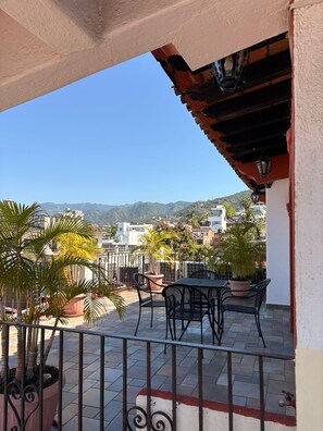 Varanda com vista para a cidade, com mesa, cadeiras, plantas em vasos e grade.