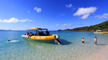 Um barco inflável amarelo com pessoas, flutuando em águas azuis cristalinas perto de uma praia.