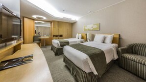 Quarto de hotel com duas camas, uma escrivaninha, uma televisão e um sofá.