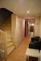 Um corredor com piso de madeira, uma escada, um sofá de couro preto e uma mesa pequena.