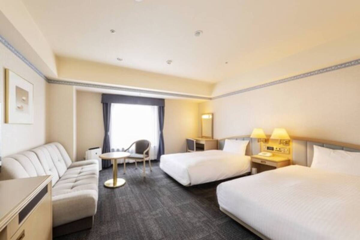 Quarto de hotel com duas camas, um sofá, uma mesinha e uma cadeira.