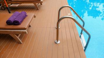 Área da piscina com espreguiçadeiras de madeira e uma escada de metal para a piscina.