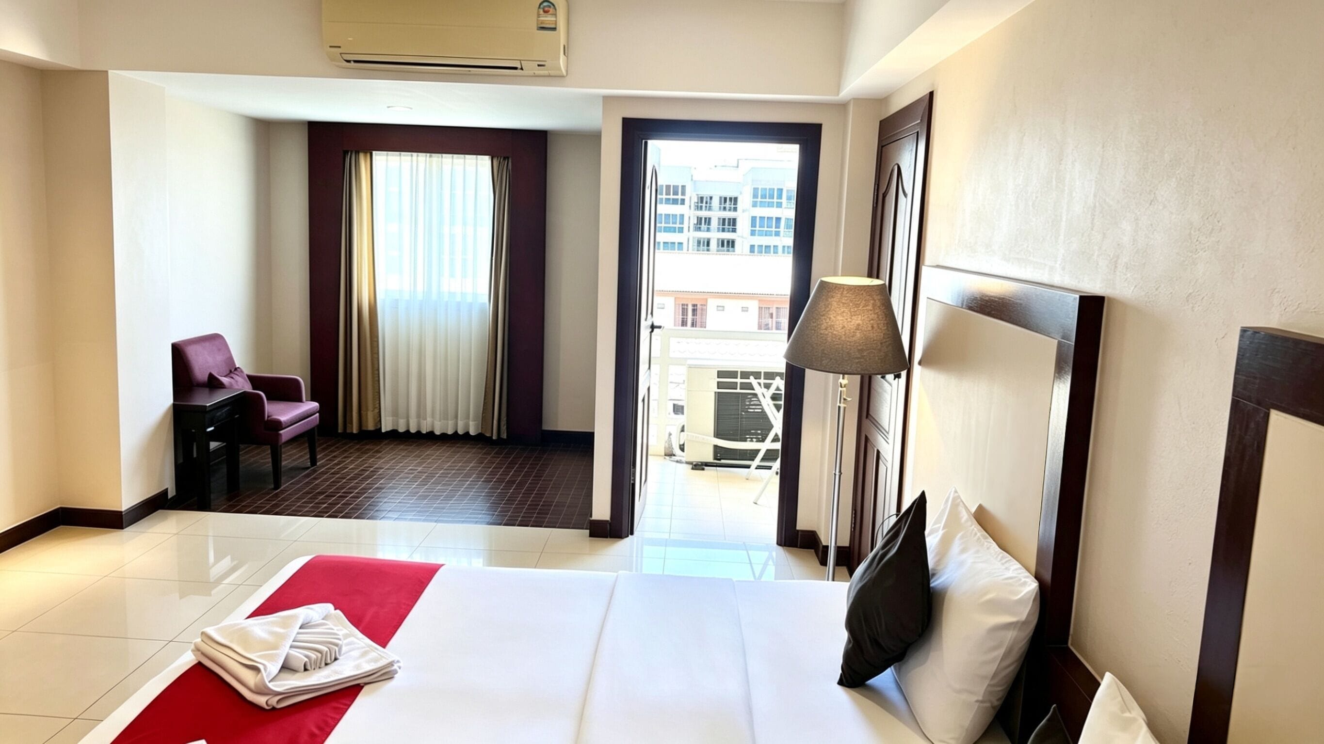 Quarto de hotel com cama, poltrona, mesa, luminária e vista para o exterior.