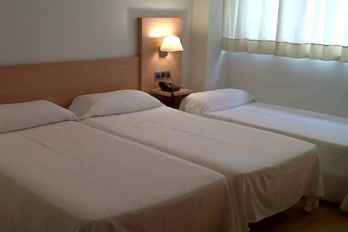 Quarto de hotel com duas camas de solteiro, mesa de cabeceira com abajur e janela com cortinas.