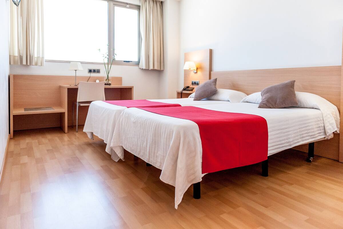 Quarto de hotel com uma cama, uma escrivaninha e uma cadeira.