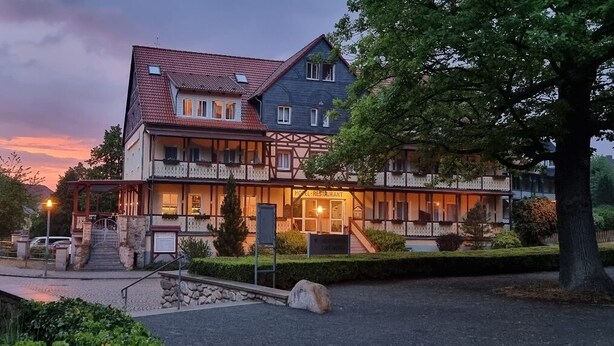 Um hotel europeu tradicional com entrada bem iluminada, varanda e um caminho de pedra que leva à porta.