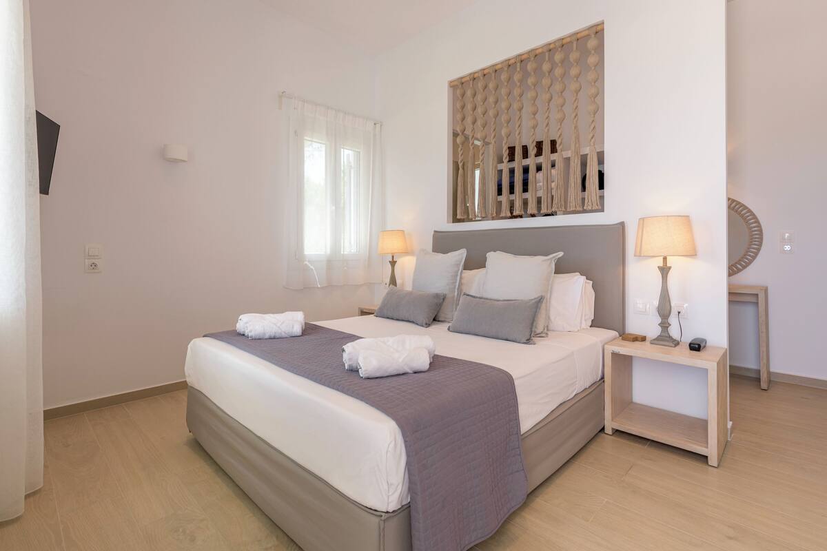 Quarto de hotel bem arrumado com cama, mesas de cabeceira, luminárias e um objeto decorativo na parede.