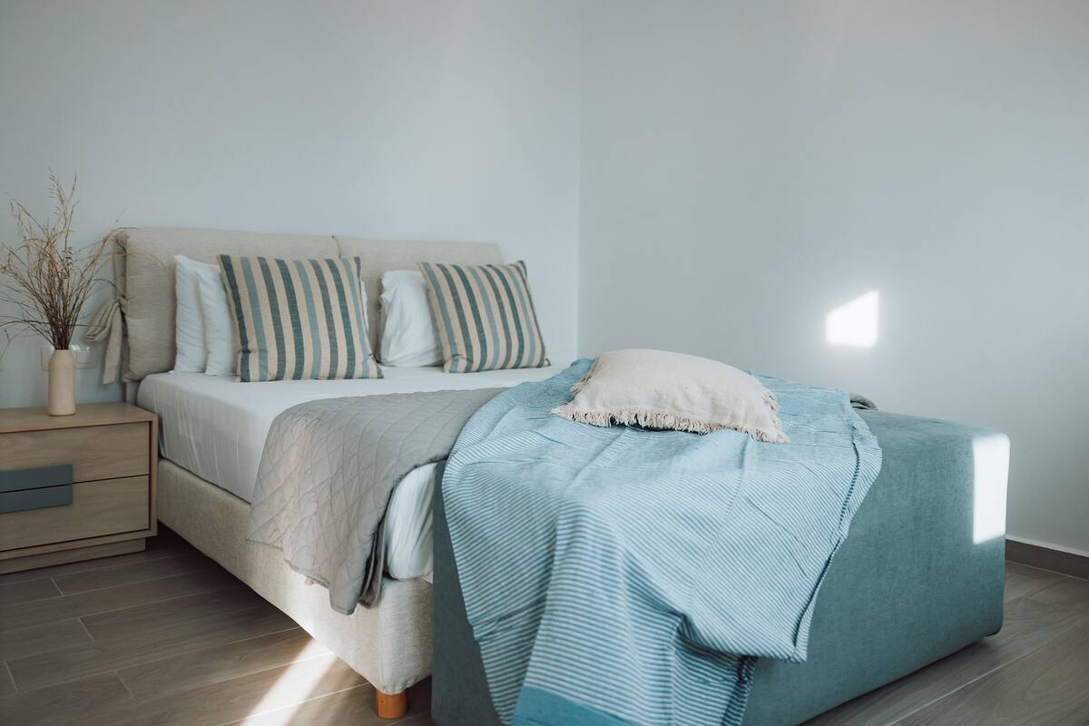 Quarto bem arrumado com cama, mesa de cabeceira e um vaso de plantas secas.
