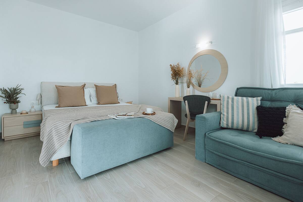 Um quarto moderno com cama, escrivaninha, cadeira, sofá e espelho.