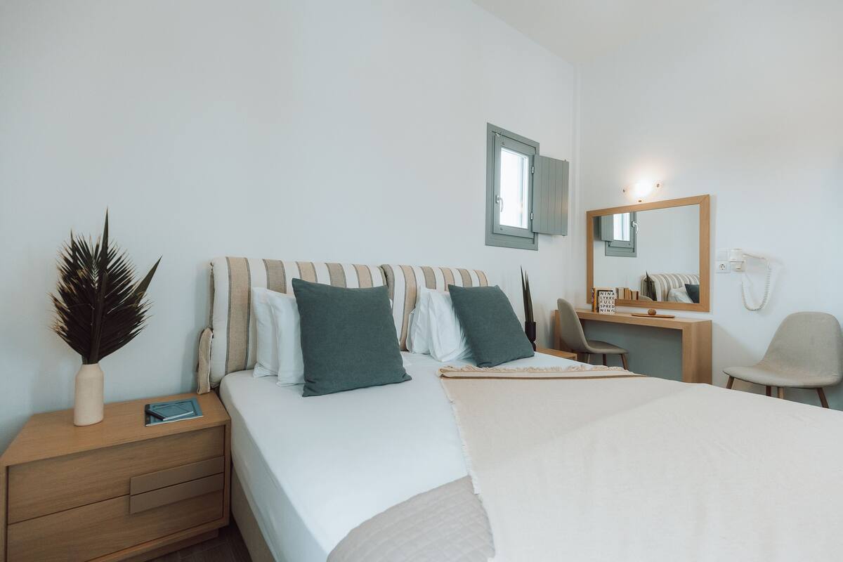 Quarto bem organizado com cama, mesa de cabeceira, cadeira, escrivaninha e espelho.