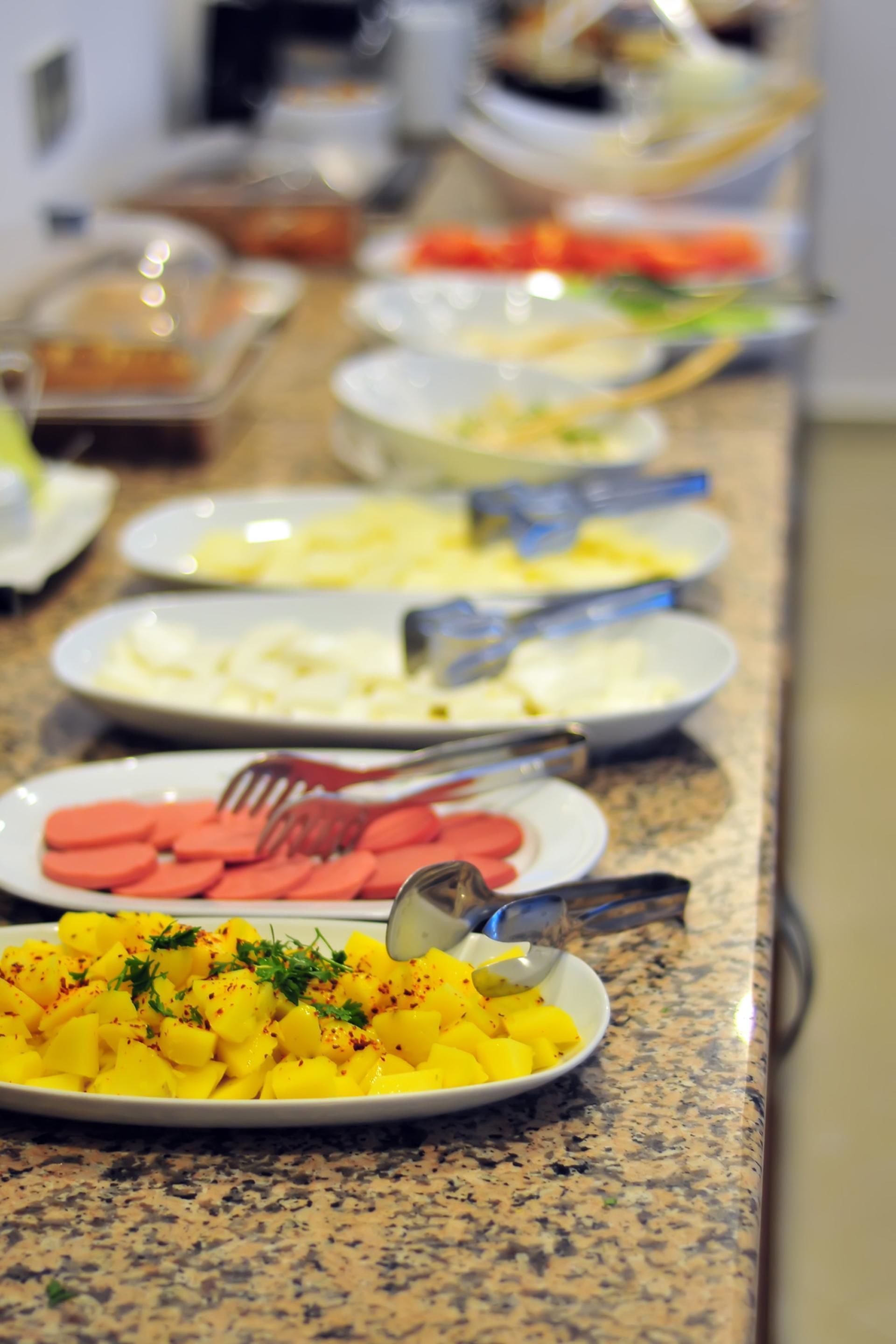 Uma mesa de buffet com diversos pratos, incluindo batatas, tomates e uma salada com ervas.