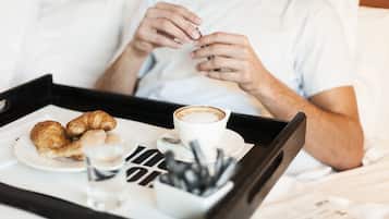 Uma bandeja com croissants, uma xícara de café e um copo de água sobre a cama.