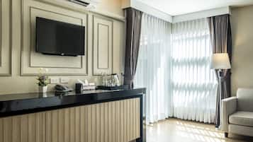 Quarto de hotel moderno com parede de painel de madeira, televisão de tela plana, escrivaninha com telefone, cafeteira e luminária.