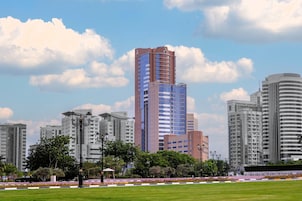 Um edifício moderno de arranha-céu com design arquitetônico único, rodeado por um parque bem cuidado com árvores e céu limpo.