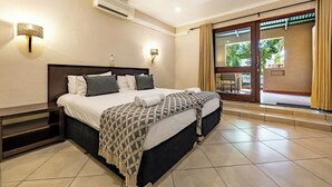 Quarto de hotel com uma cama grande, duas luminárias de cabeceira, uma mesinha de noite e vista para o exterior por uma porta de vidro deslizante.