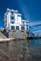 Um edifício branco com varandas azuis, base de pedra e céu azul límpido.
