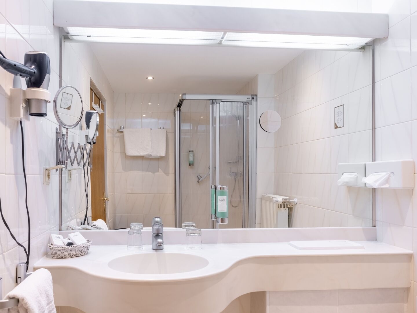 Uma casa de banho moderna com um espelho grande, uma pia, um chuveiro e um secador de cabelo.