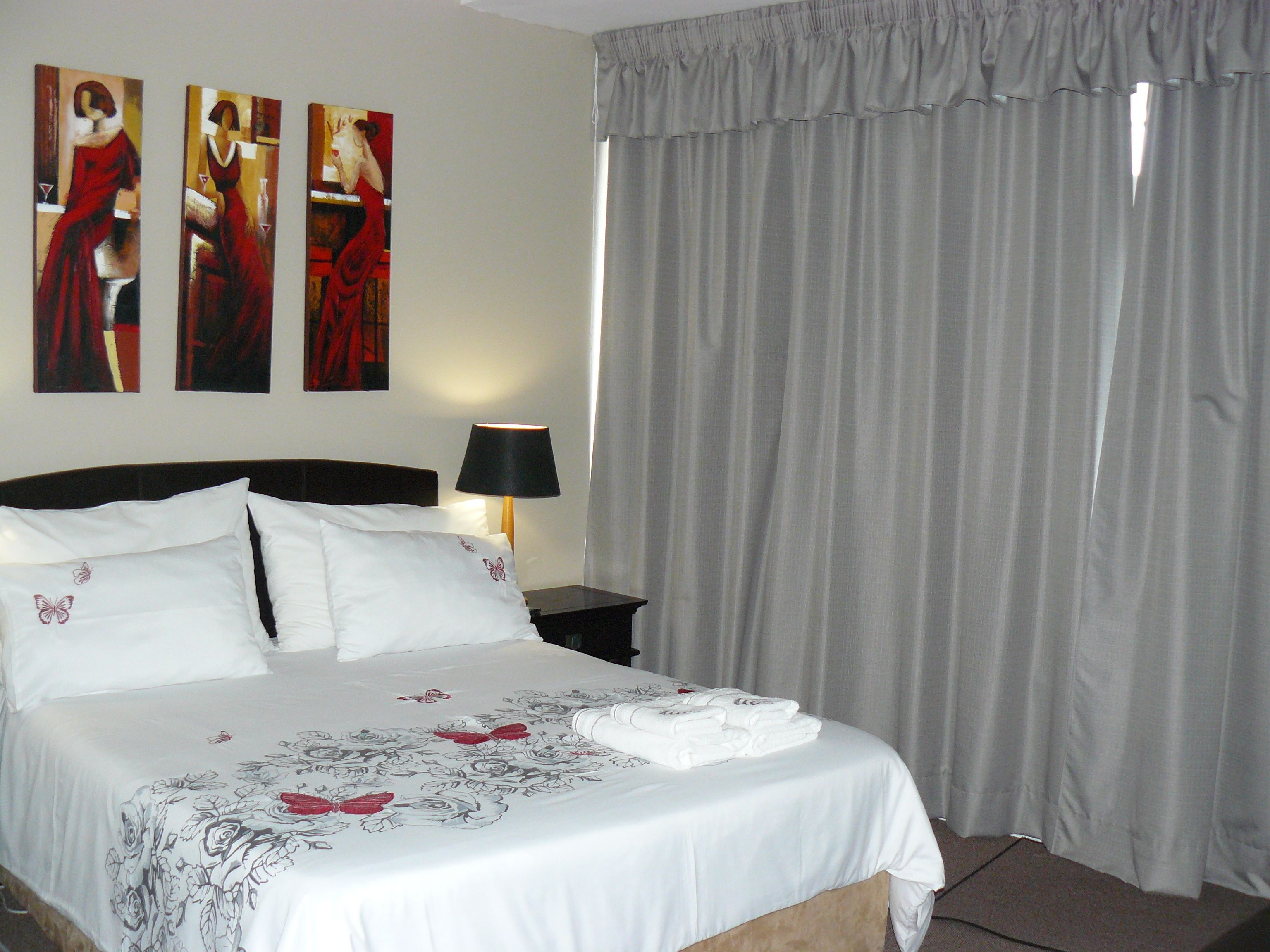Quarto de hotel com cama, mesa de cabeceira, luminária e três quadros na parede.