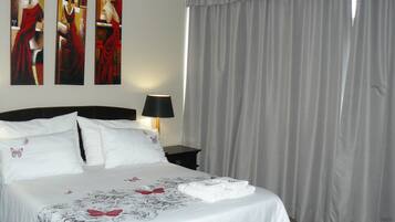 Quarto de hotel com cama, mesa de cabeceira, luminária e três quadros na parede.