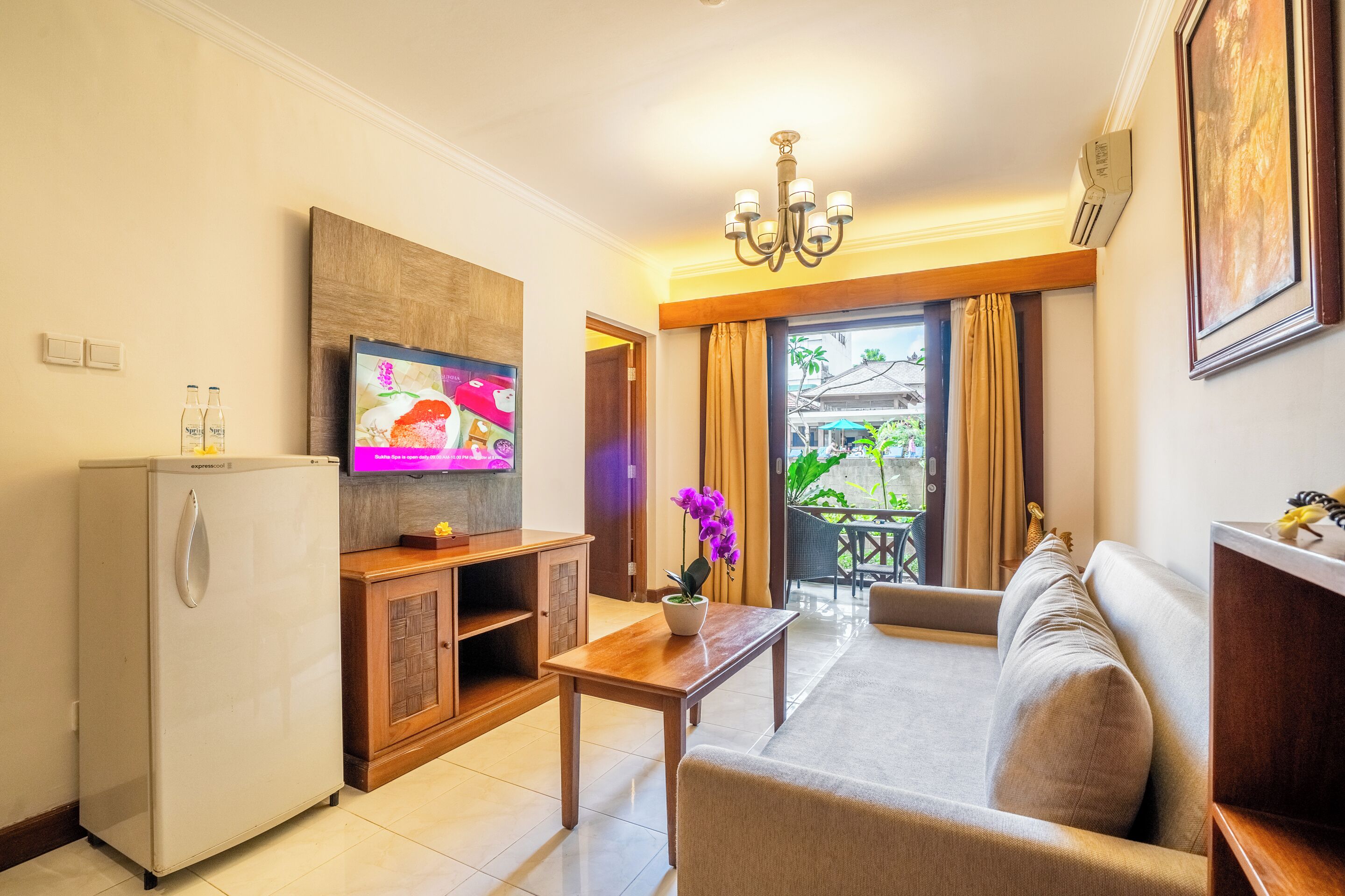 Uma sala de estar com sofá, televisão, uma mesinha e geladeira.