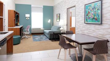 Quarto de hotel moderno com cozinha compacta, área de refeições, sofá e uma grande pintura abstrata.