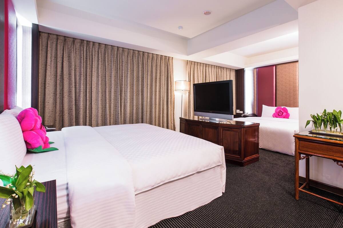 Quarto de hotel com uma cama grande, televisão, escrivaninha e mesa de cabeceira.