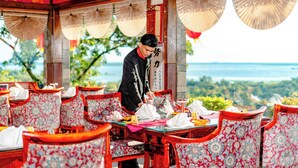 Um restaurante com decoração tradicional chinesa, mesas ao ar livre e vista para o mar.