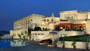 Um hotel grande, com vários andares, piscina, área de estar ao ar livre e um jardim bem cuidado.