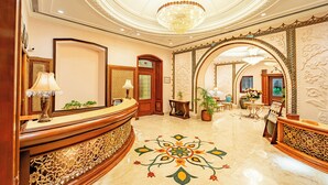 Um saguão com balcão de recepção, decoração de parede elaborada, um lustre e piso estampado.