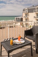 Uma varanda com uma mesa, uma cadeira e vista para a praia e o oceano.