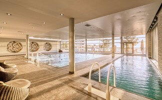Uma grande piscina coberta com água cristalina, rodeada por espreguiçadeiras e um chão revestido de azulejos.