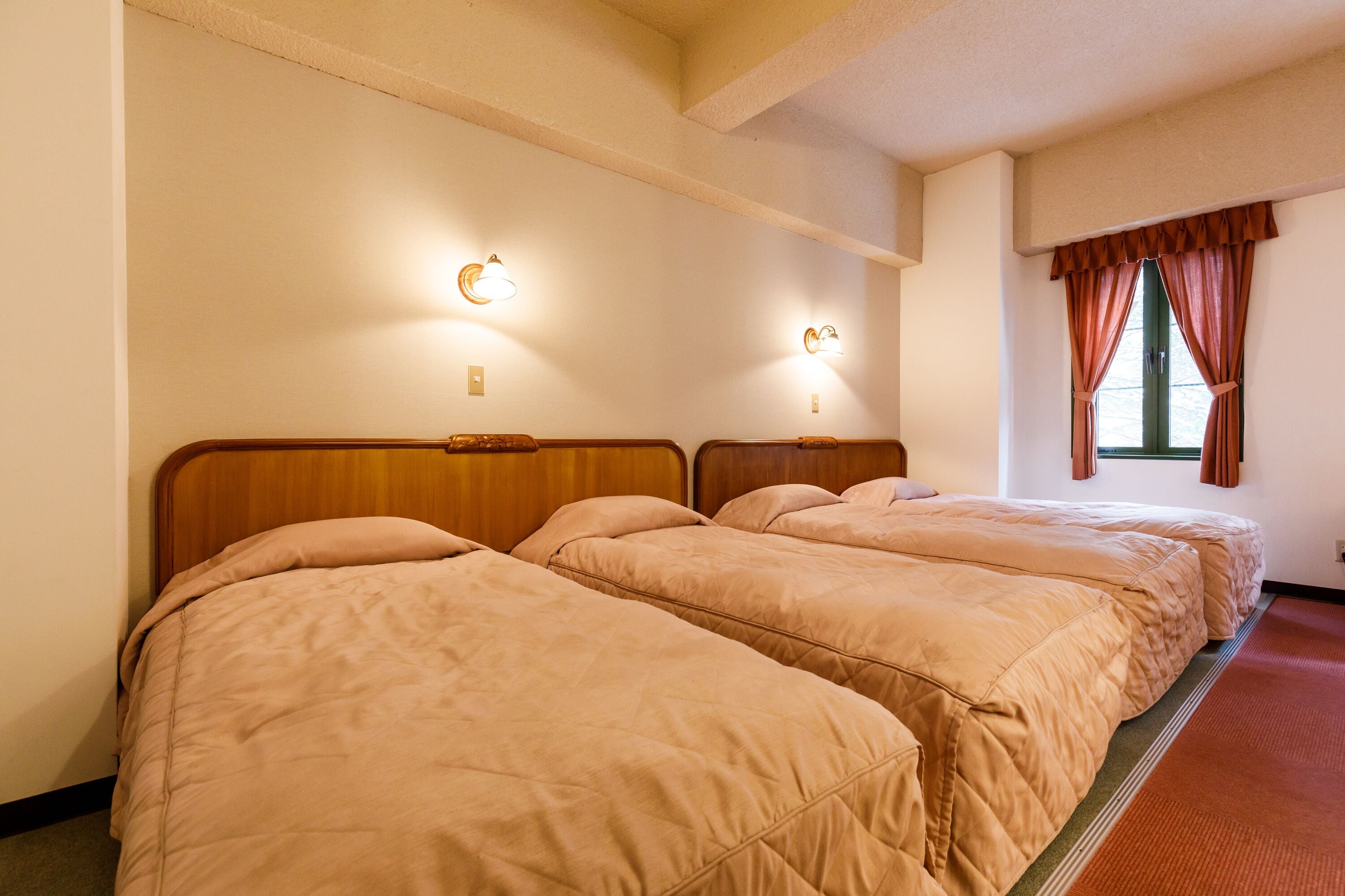 Quarto de hotel com duas camas, cabeceiras de madeira e luminárias fixadas na parede.