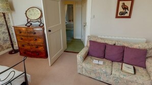 Quarto com cômoda de madeira, sofá estampado, quadro na parede e porta que dá para outro espaço.