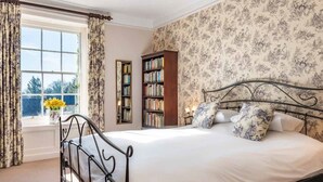 Quarto com uma cama grande, uma estante de livros e uma janela com cortinas.