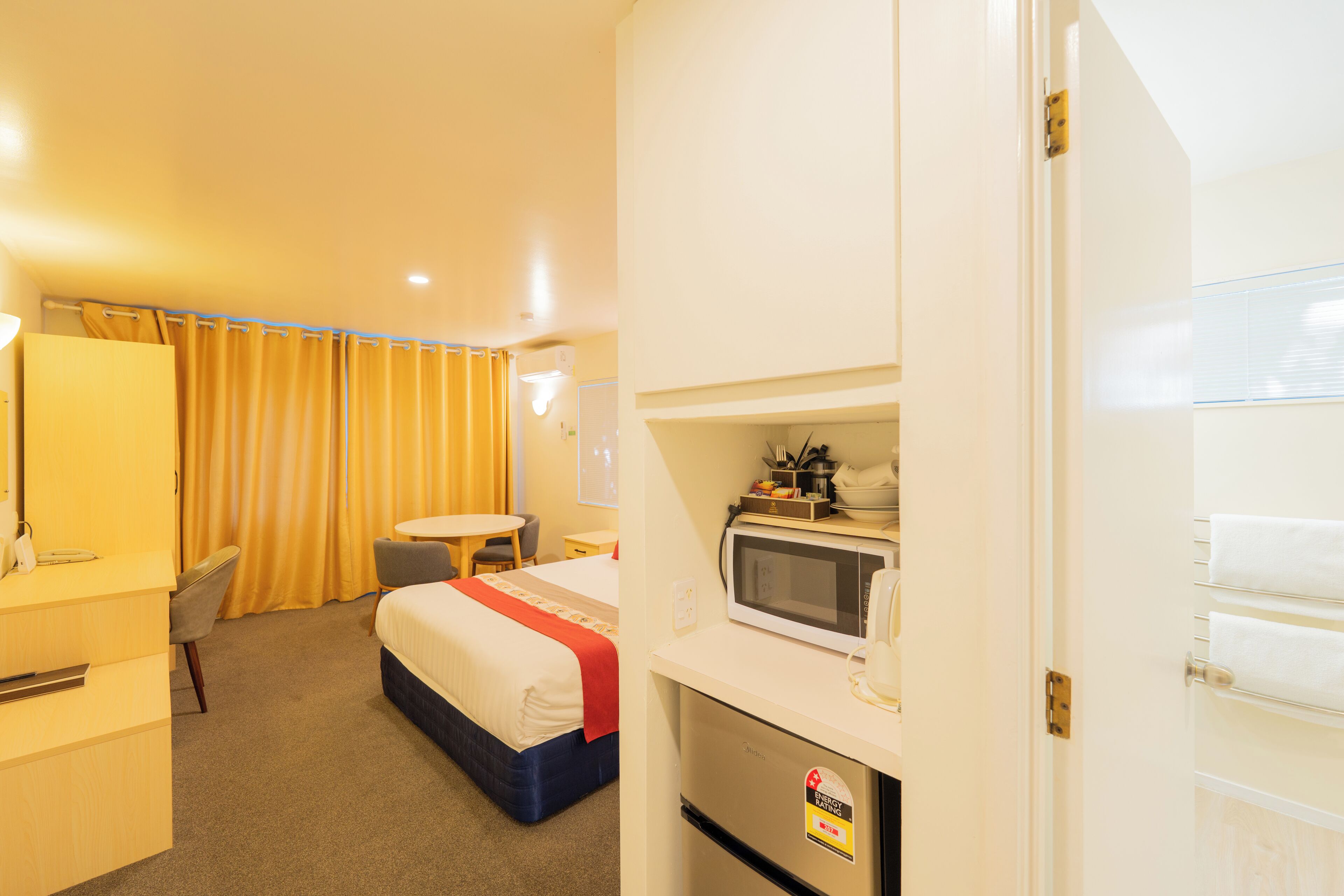 Quarto de hotel com cama, escrivaninha, cadeira, micro-ondas e frigorífico.