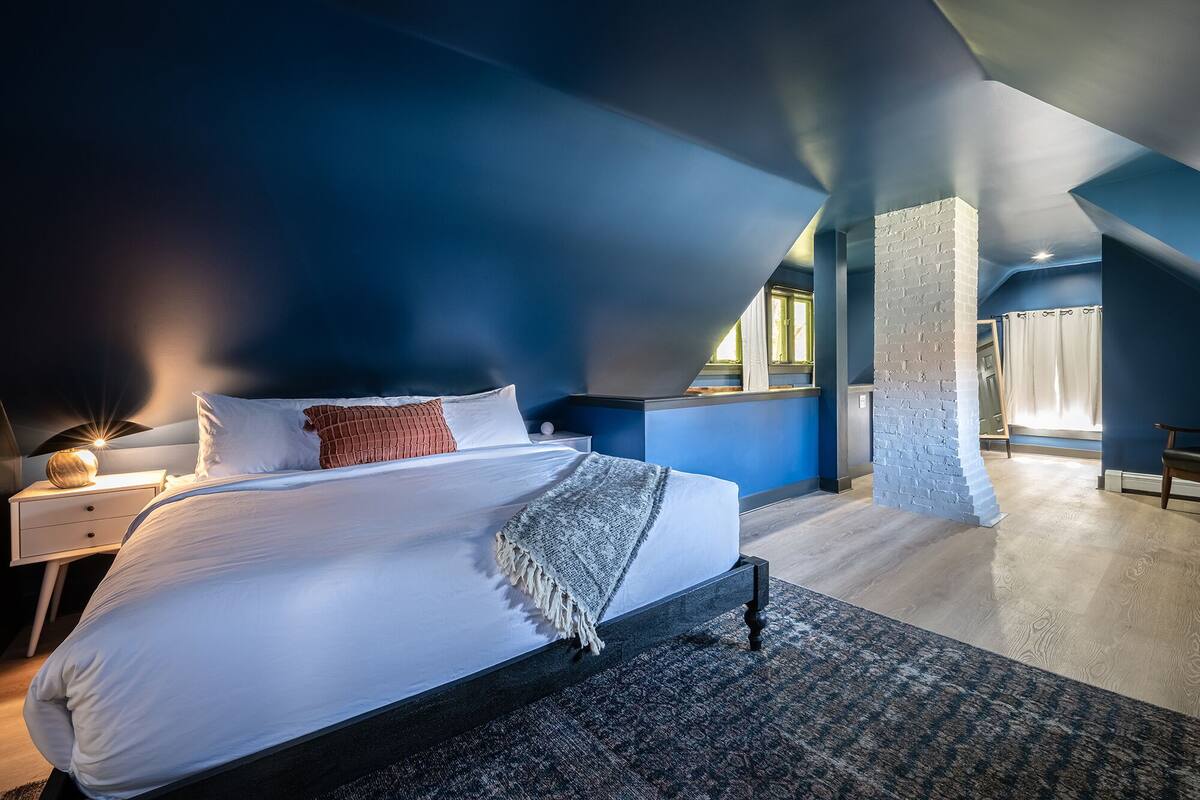 Quarto moderno com uma cama grande, mesa de cabeceira, abajur e um pilar de pedra.