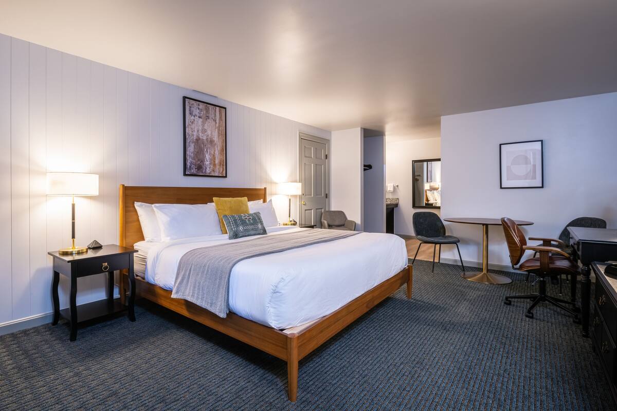 Quarto de hotel com uma cama grande, mesas de cabeceira, escrivaninha e cadeiras.