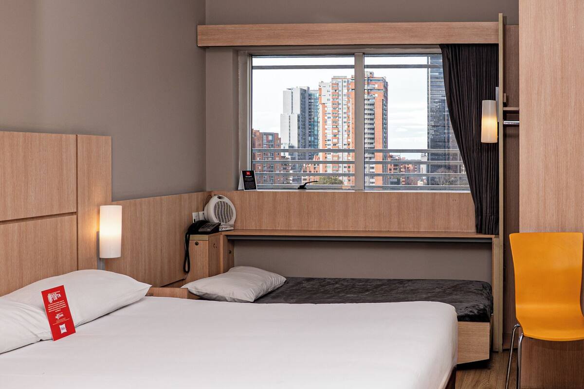 Quarto de hotel moderno com uma cama grande, uma escrivaninha, uma cadeira, uma janela com vista para a cidade e um aquecedor embutido.