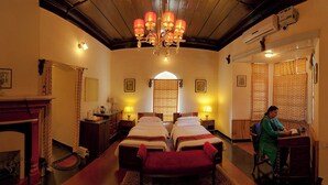 Quarto de hotel com duas camas, lareira, escrivaninha e uma pessoa trabalhando.