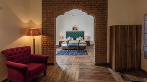 Quarto com arco de tijolos que dá para uma cama com cabeceira verde, uma poltrona vermelha e um armário de madeira.