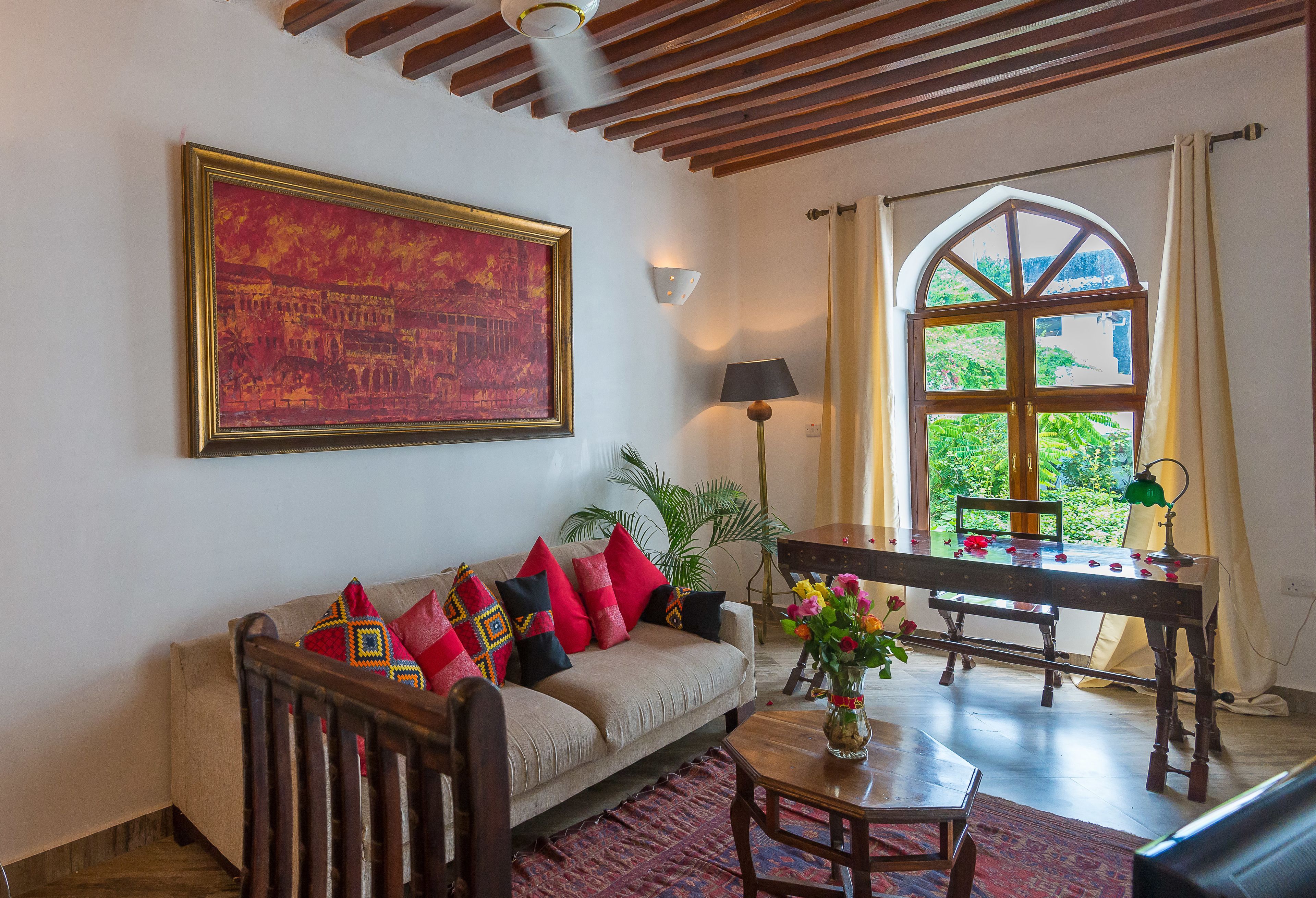 Uma sala de estar com sofá, mesa, luminária e uma grande janela com cortinas.