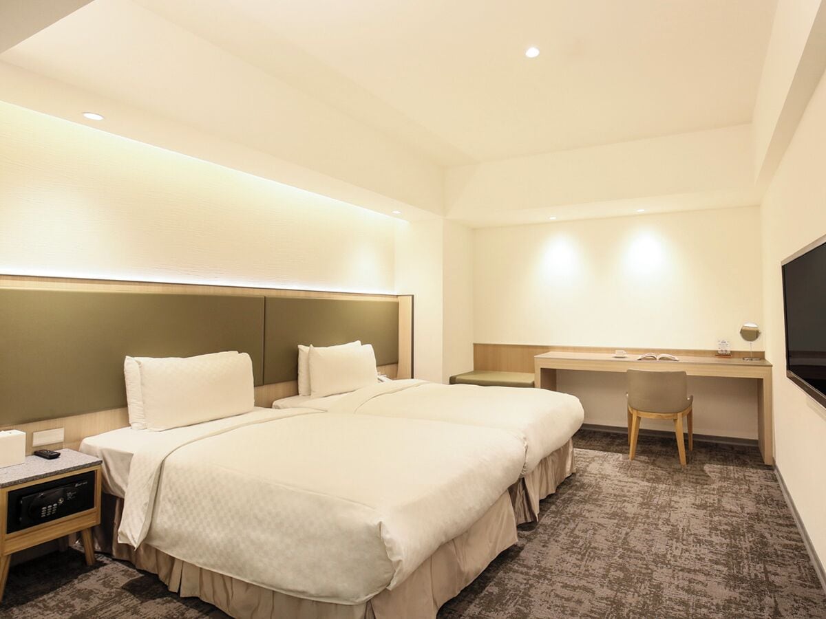 Quarto de hotel com uma cama grande, uma escrivaninha e uma televisão.