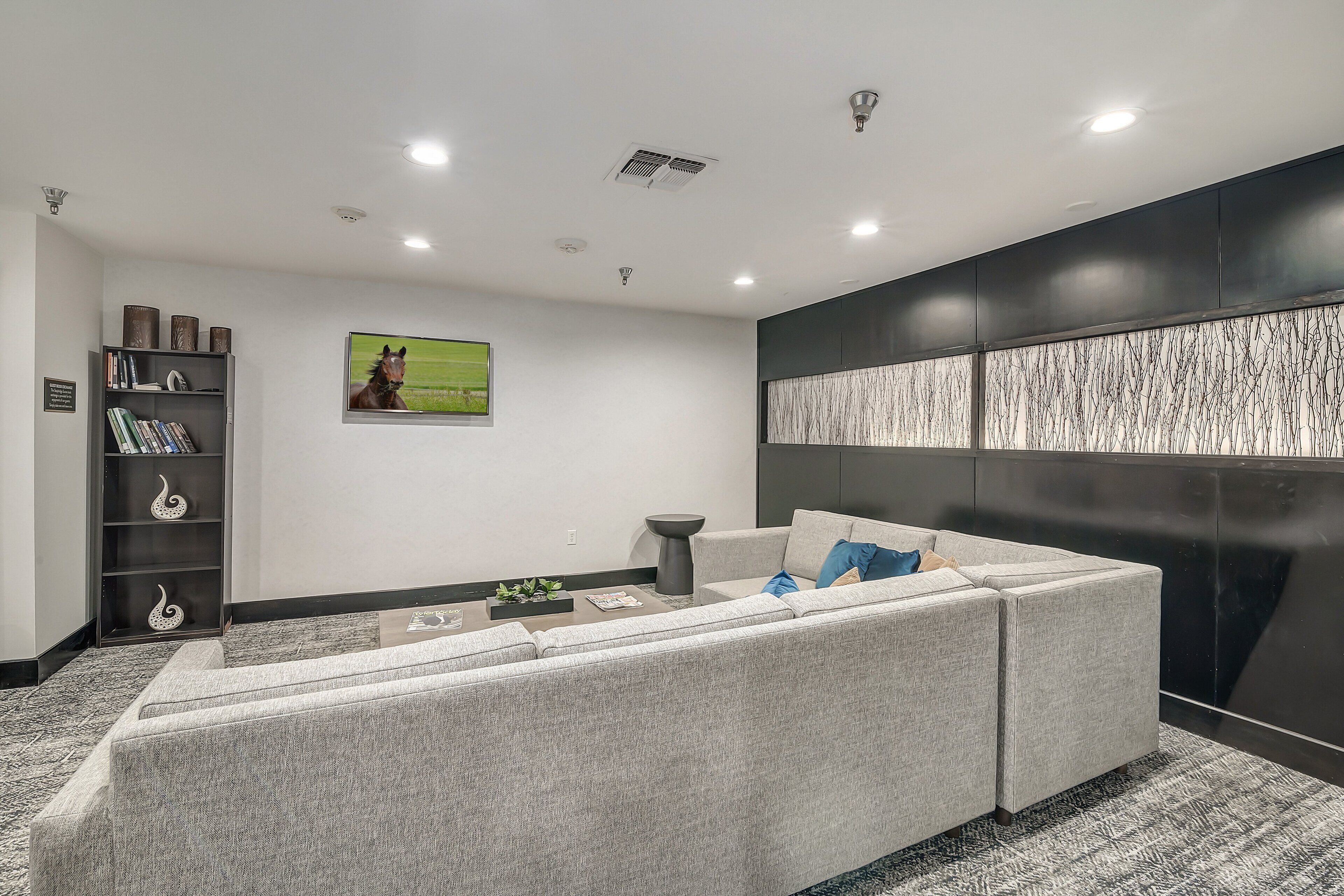 Uma sala de estar moderna com um sofá modular cinza, uma estante, uma moldura com a imagem de um cavalo e um painel decorativo na parede.