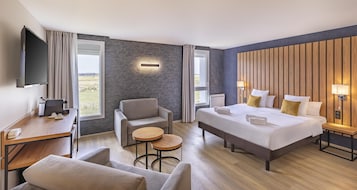 Quarto de hotel com cama, escrivaninha, cadeira, mesinha e televisão.