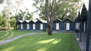 Uma fileira de cabanas azuis com portas brancas, rodeadas por um gramado bem cuidado e árvores.