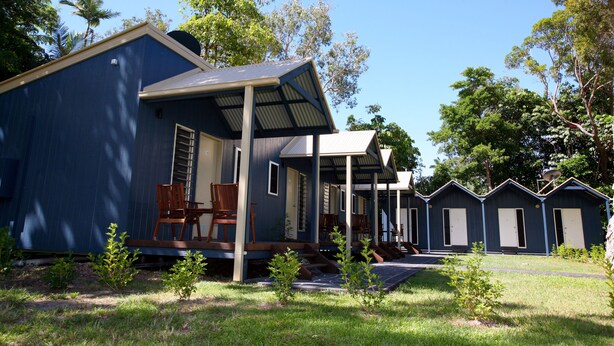 Uma fileira de cabanas azuis com varanda coberta e um pequeno jardim frontal.