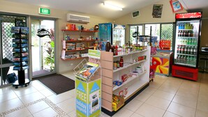 Interior de loja com prateleiras repletas de produtos diversos, uma geladeira com bebidas e um sinal de saída.