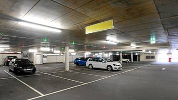 Garagem subterrânea de vários níveis com vários carros estacionados, pilares de concreto e iluminação fluorescente no teto.