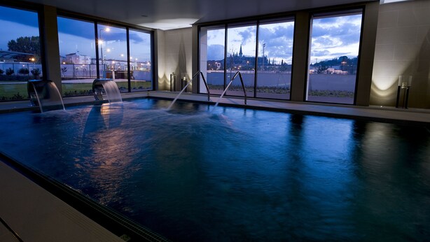 Piscina interna com vista para a paisagem urbana através de grandes janelas.